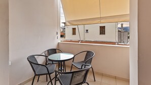 Uma varanda com mesa e cadeiras, um toldo bege e vista para edifícios.