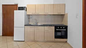 Uma cozinha com armários de madeira clara, geladeira branca, fogão preto e painel de azulejos.