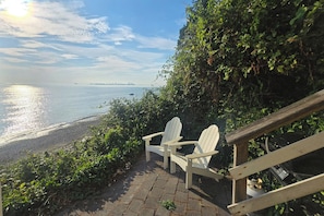 Escada de madeira que dá para uma praia, com duas cadeiras Adirondack.