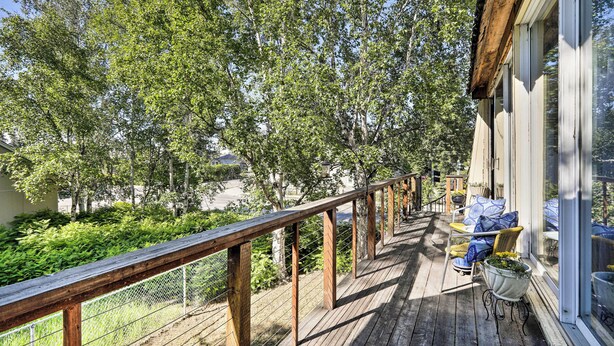 Um deck de madeira com guarda-corpo, com vista para um jardim e árvores.