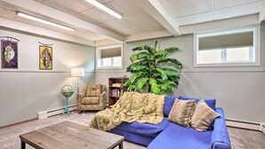 Uma sala de estar com um sofá azul, uma mesa de centro de madeira, um globo em um suporte, uma estante de livros e uma planta grande.