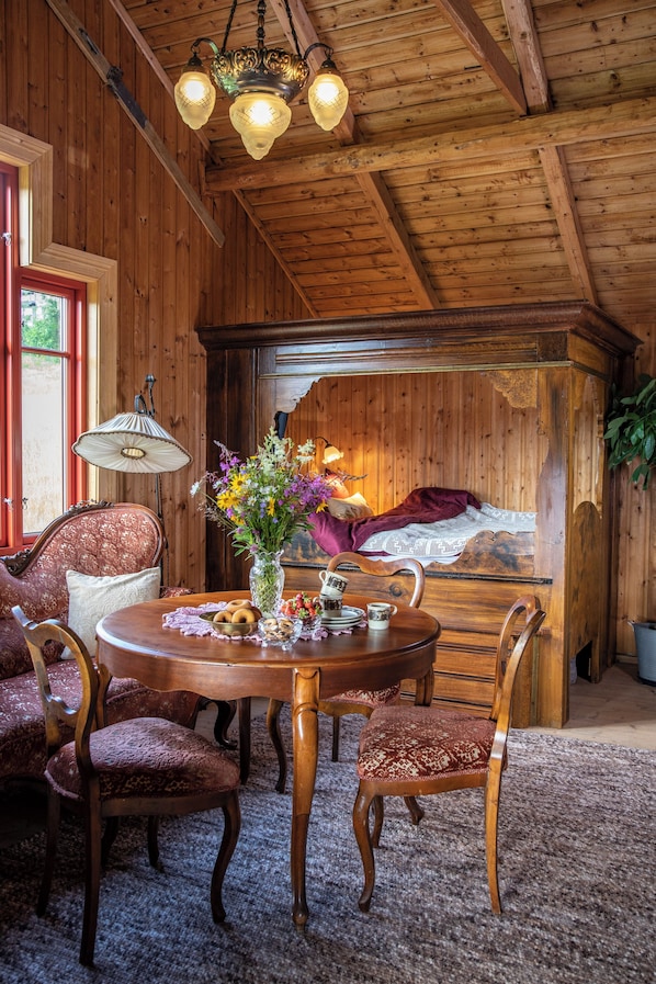 Uma sala de jantar de madeira com uma mesa redonda, cadeiras, um vaso com flores e um abajur.