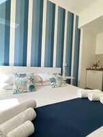 Quarto de hotel com parede listrada, cama com roupa de cama branca e colcha azul.