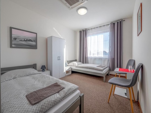 Quarto de hotel com duas camas, uma escrivaninha, uma cadeira, um guarda-roupa e uma janela com cortinas.