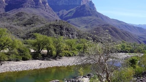 Um rio com margens rochosas e vegetação escassa, cercado por montanhas íngremes e pedregosas.