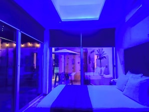 Quarto com cama, porta de vidro para varanda e vista exterior.