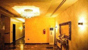 Corredor de hotel com lustre, extintor de incêndio, espelho e unidade de ar condicionado na parede.