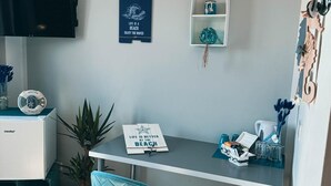 Quarto compacto com escrivaninha, duas cadeiras, cafeteira e um pequeno armário com objetos decorativos.