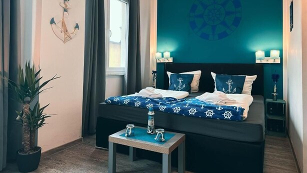 Quarto com cama, mesa de cabeceira, planta em vaso e parede com decoração náutica.