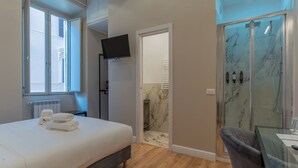 Quarto com cama, televisão, chuveiro e mesa de vidro.