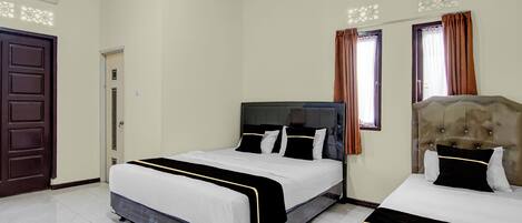 Quarto de hotel com uma cama grande, uma cama menor, um guarda-roupa, uma porta e uma janela com cortinas.