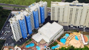 Um hotel de grande porte com vários edifícios azul e bege, um pátio central com piscinas e uma área de estacionamento.