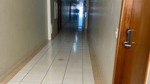 Um corredor comprido e estreito com chão de azulejos e uma porta de madeira à direita.