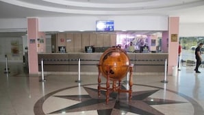 Um hall com design de piso em formato de bússola, um balcão de recepção e uma tela de televisão acima.