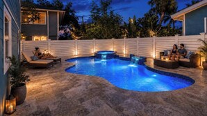 Piscina com cachoeira, cercada por grade branca, e equipada com espreguiçadeiras e ofurô.