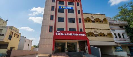 Um hotel com vários andares e fachada em vermelho e bege, com a placa 'Sri Balaji Grand Hotel' e 'FabHotels'.