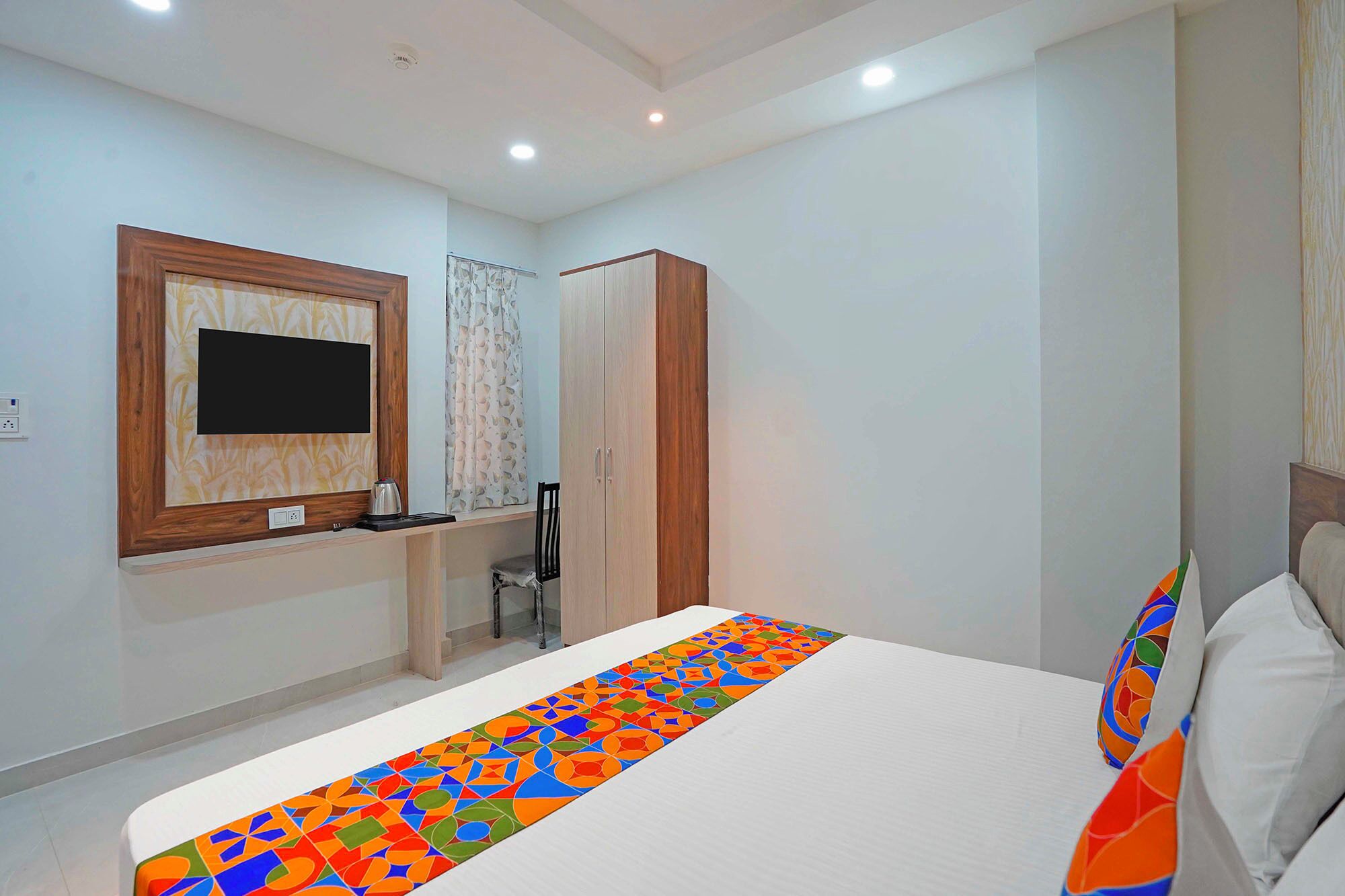 Quarto de hotel com cama, televisão na parede, secretária com cadeira e guarda-roupa.