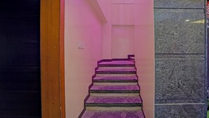 Escada com corrimão de madeira e parede iluminada em rosa.