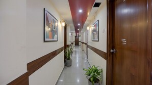 Corredor de hotel com painéis de madeira, plantas em vasos, obras de arte emolduradas e teto vermelho.