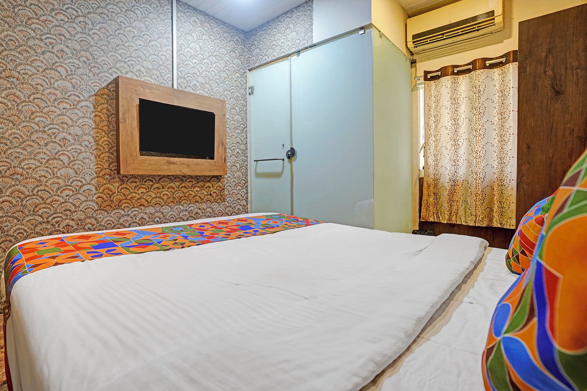 Quarto de hotel com uma cama, guarda-roupa, televisão na parede e cortina.