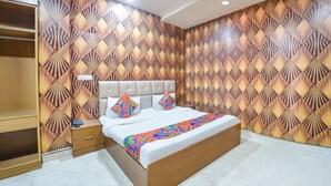 Quarto com papel de parede estampado, cama com colcha colorida, mesa de cabeceira com telefone e criado-mudo.