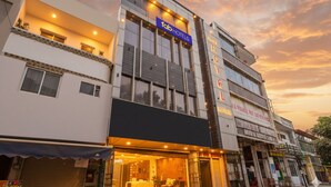 Um edifício de vários andares com a placa 'fab hotels', apresentando uma fachada moderna com grandes janelas e uma varanda.
