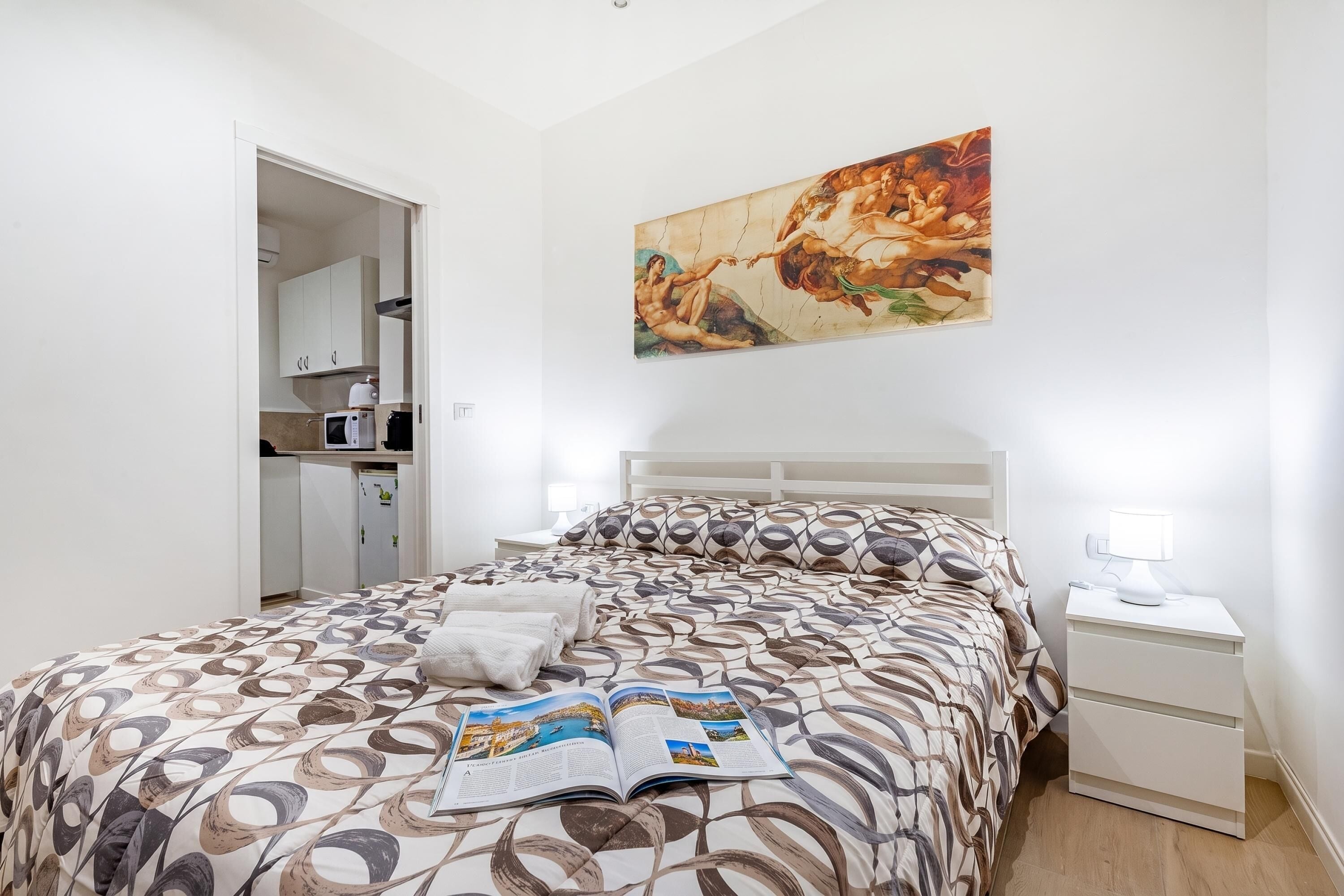 Quarto com cama, mesa de cabeceira, material de leitura e um quadro na parede.