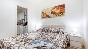 Quarto com cama, mesa de cabeceira, material de leitura e um quadro na parede.