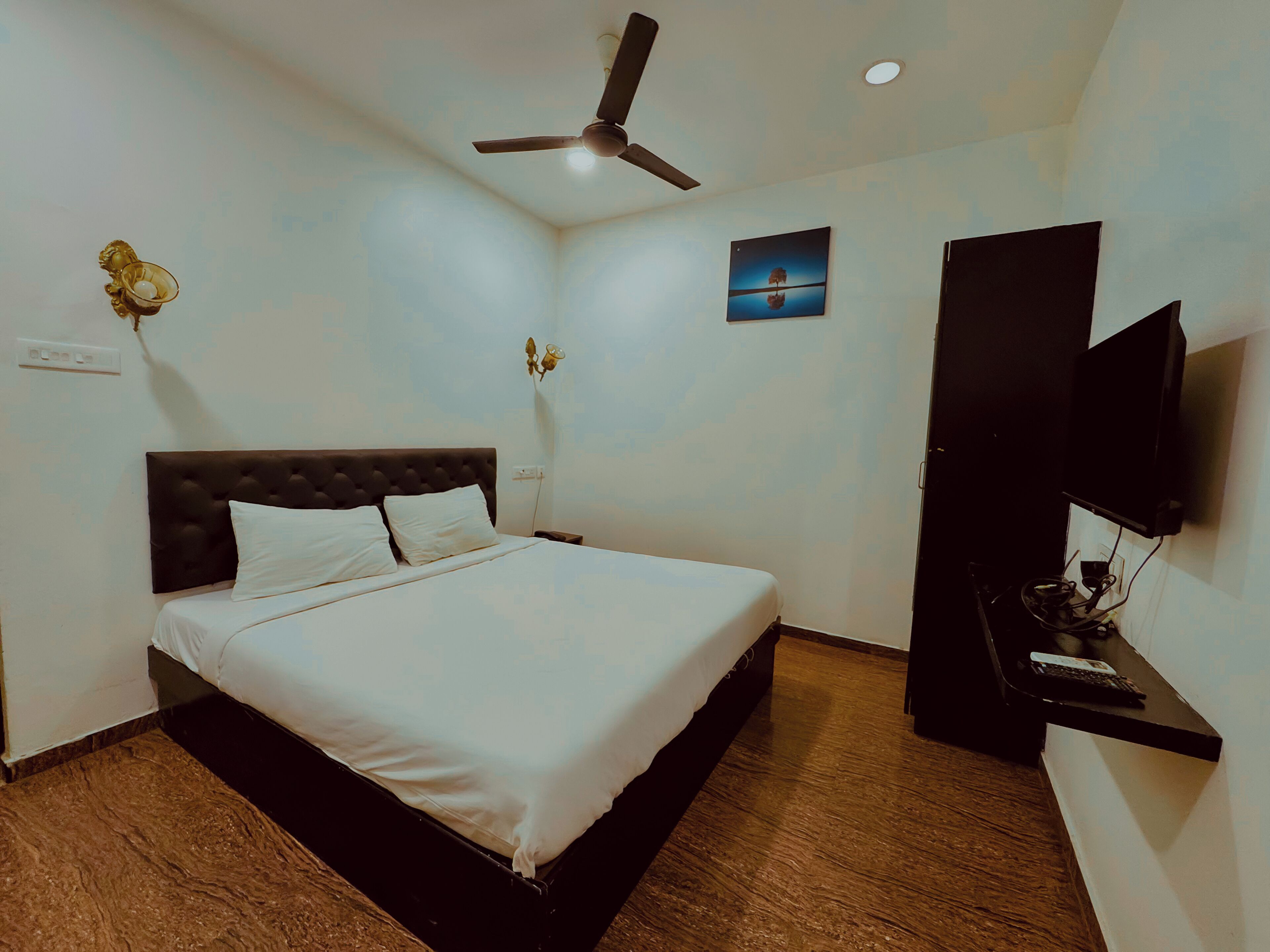 Quarto com cama, ventoinha no teto, televisão fixada na parede e mesa de cabeceira.