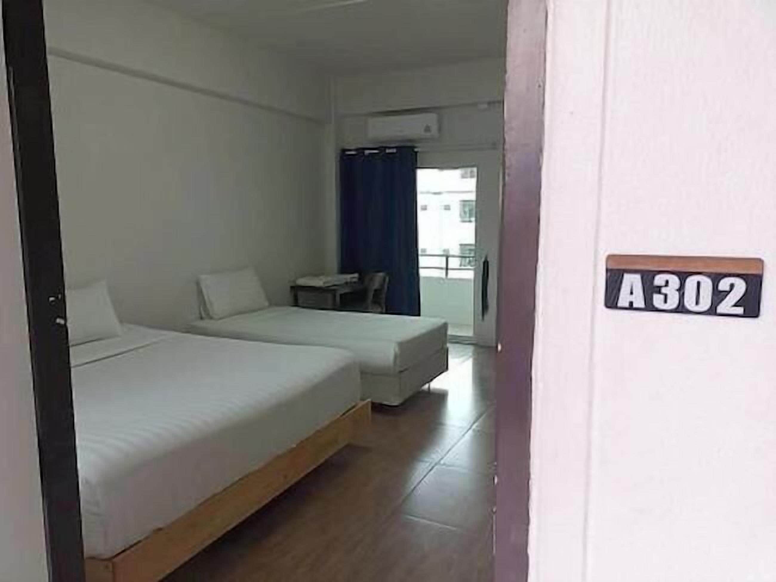 Quarto com duas camas, uma mesinha e uma cadeira. Há uma placa na parede com o número A302.