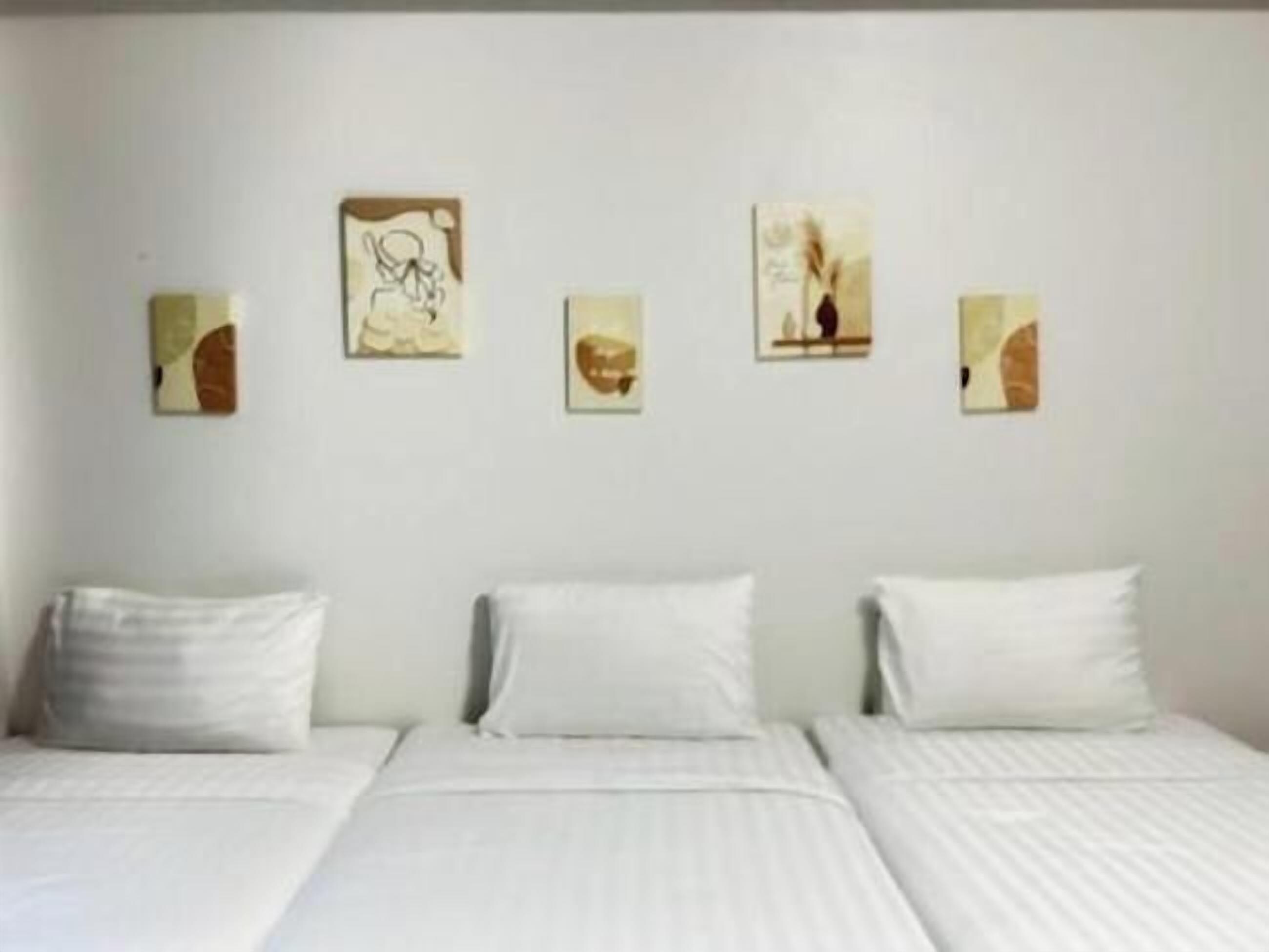 Quarto de hotel com três camas, cada uma com lençóis brancos. Há quatro obras de arte emolduradas na parede acima das camas.