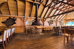 Interior rústico com vigas de madeira, lareira de pedra e peles de animais nas paredes.