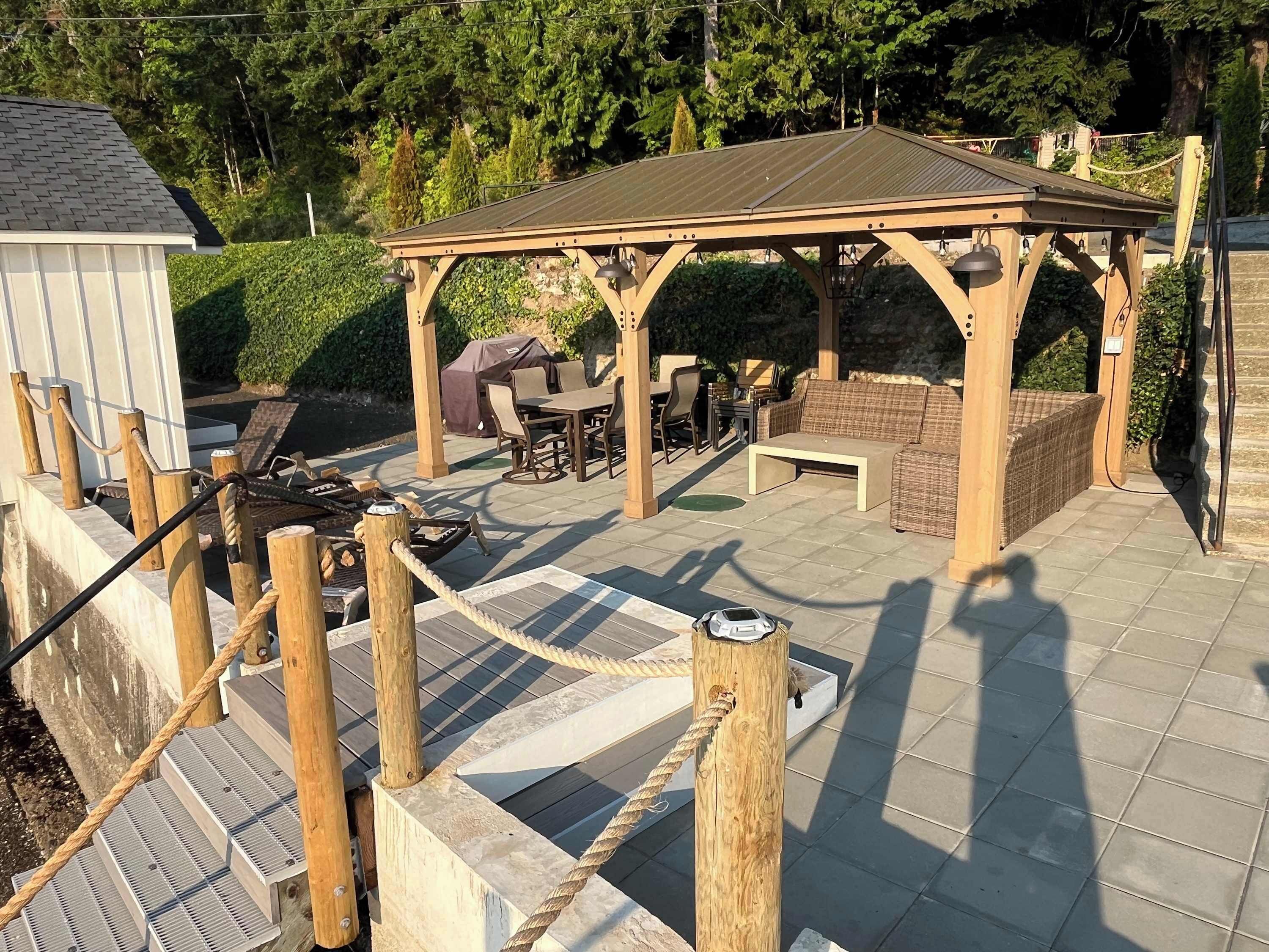 Uma área de estar coberta ao ar livre, com pérgola, mesa, cadeiras e churrasqueira.