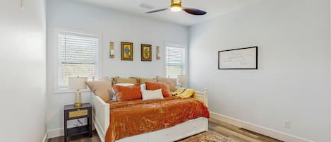 Um quarto com uma cama, uma mesinha de cabeceira, um ventilador de teto e um tapete.