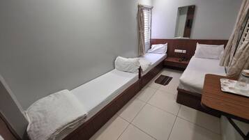 Quarto de hotel compacto com duas camas de solteiro, uma mesinha, espelho e janela com cortinas.