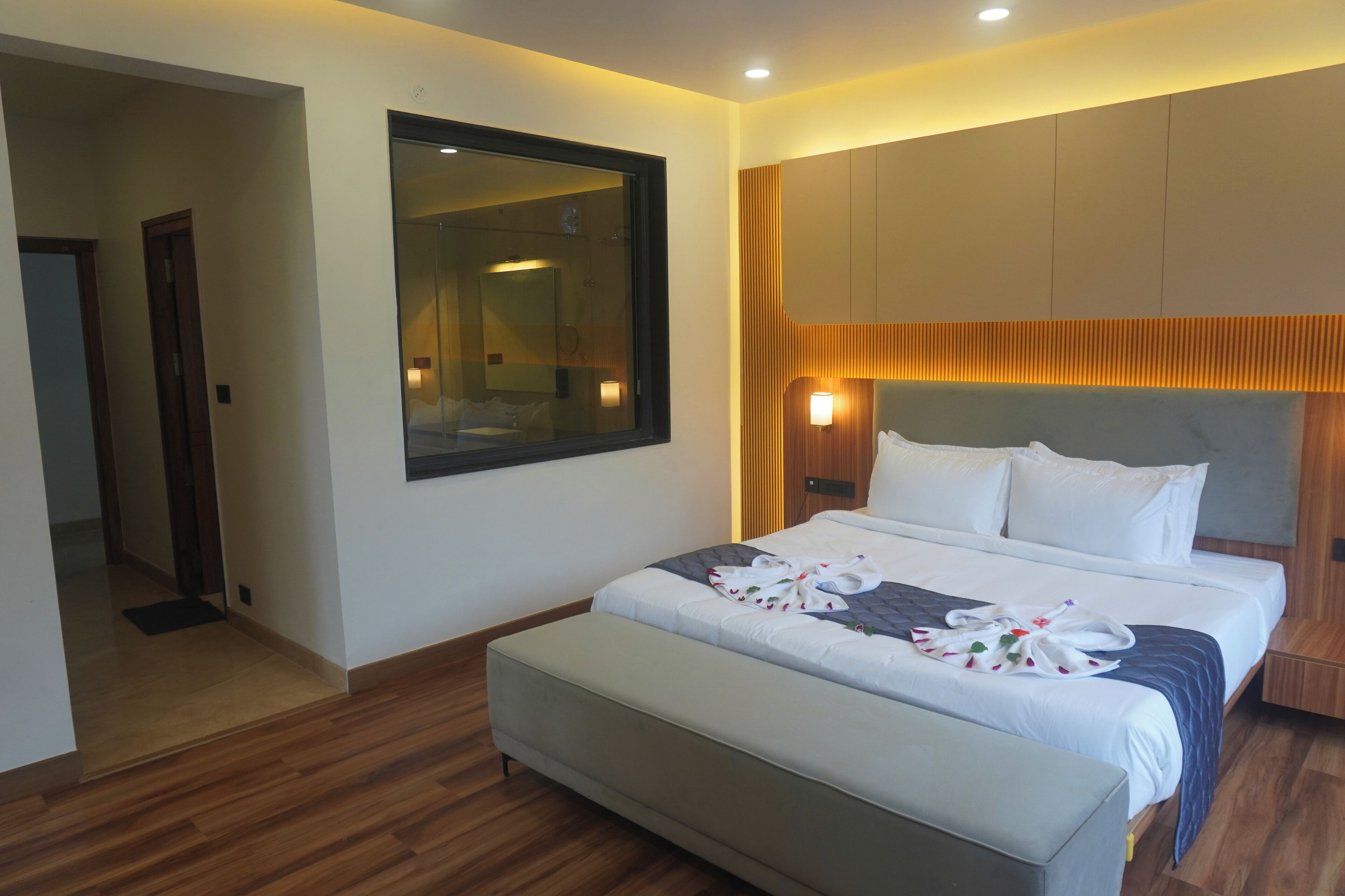 Quarto de hotel com uma cama grande, uma mesa de cabeceira, um espelho e piso de madeira.