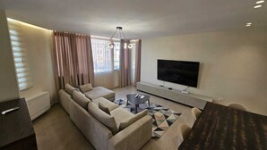 Uma sala de estar moderna com um sofá modular, uma TV de tela plana e uma mesa de jantar.