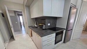 Uma cozinha moderna com armários cinzentos, bancada preta, forno embutido e geladeira de aço inoxidável.