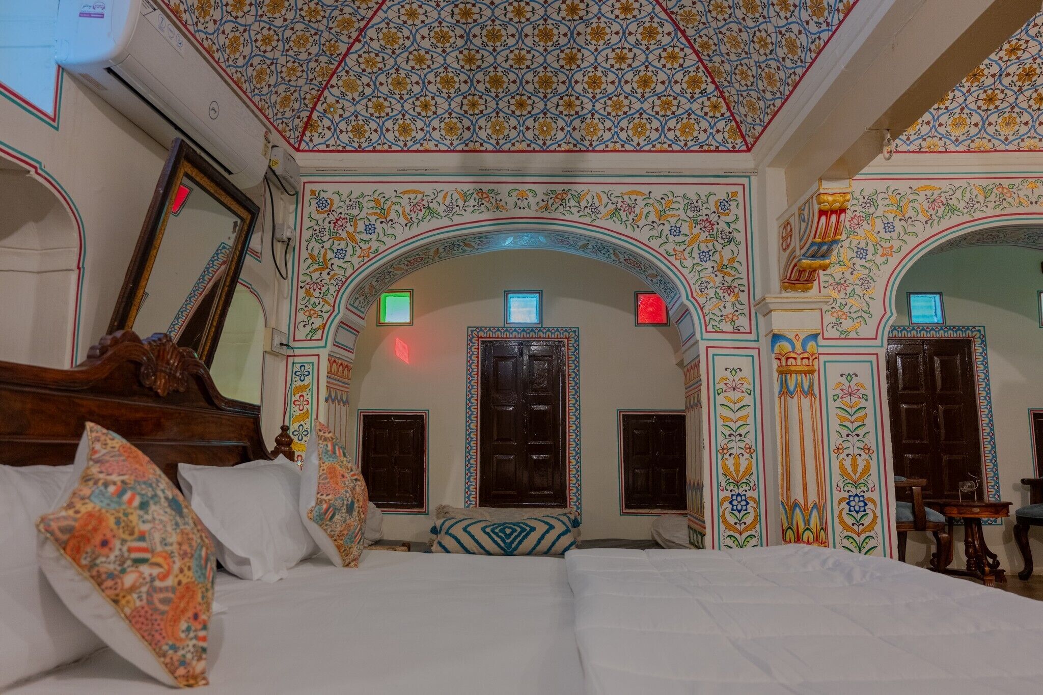 Quarto com cama, cabeceira de madeira, espelho e detalhe decorativo no teto.