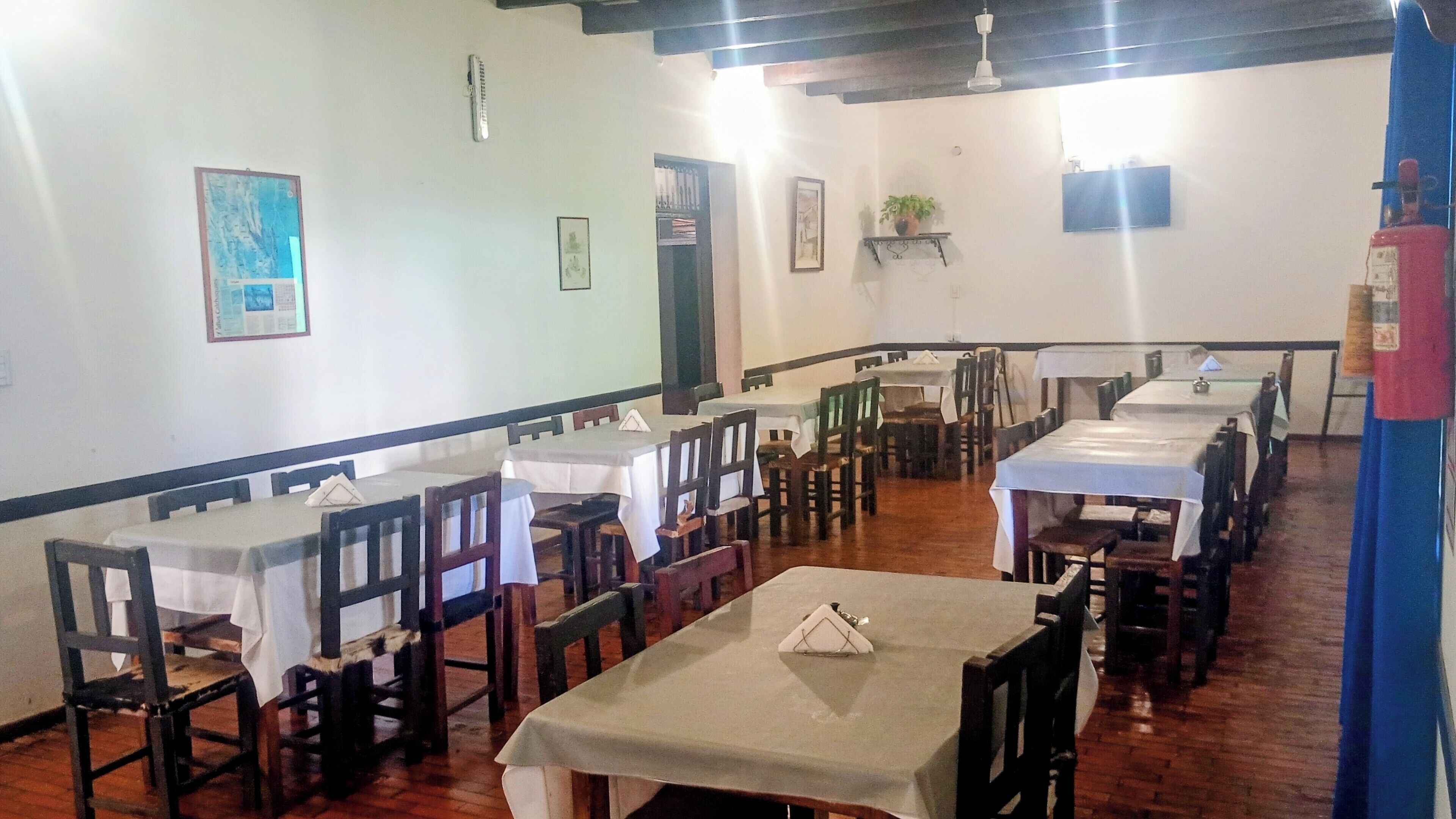 Uma sala de jantar com várias mesas e cadeiras, toalhas de mesa brancas e quadros nas paredes.
