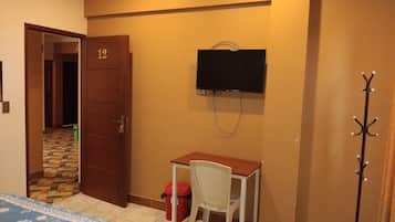 Quarto de hotel com cama, escrivaninha, televisão e cabideiro.