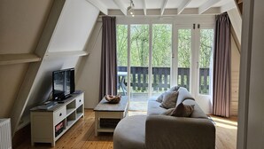 Quarto moderno estilo loft com teto inclinado, uma grande porta de correr de vidro que dá para um deck, um sofá e uma TV em um armário de madeira.