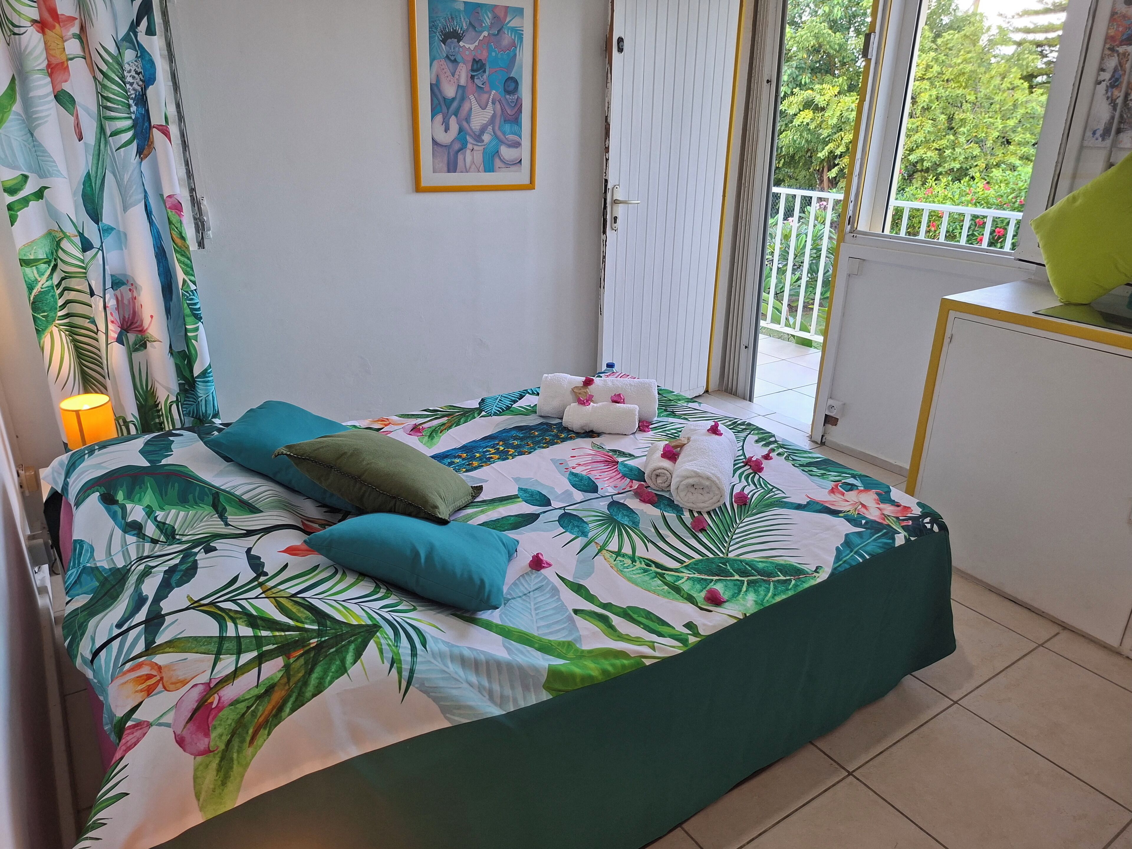 Quarto com cama, almofadas, um quadro e vista para o verde lá fora.