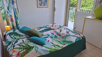 Quarto com cama, almofadas, um quadro e vista para o verde lá fora.