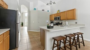Uma cozinha moderna com ilha central, armários de madeira, eletrodomésticos de aço inoxidável e um espaço com banquetas.