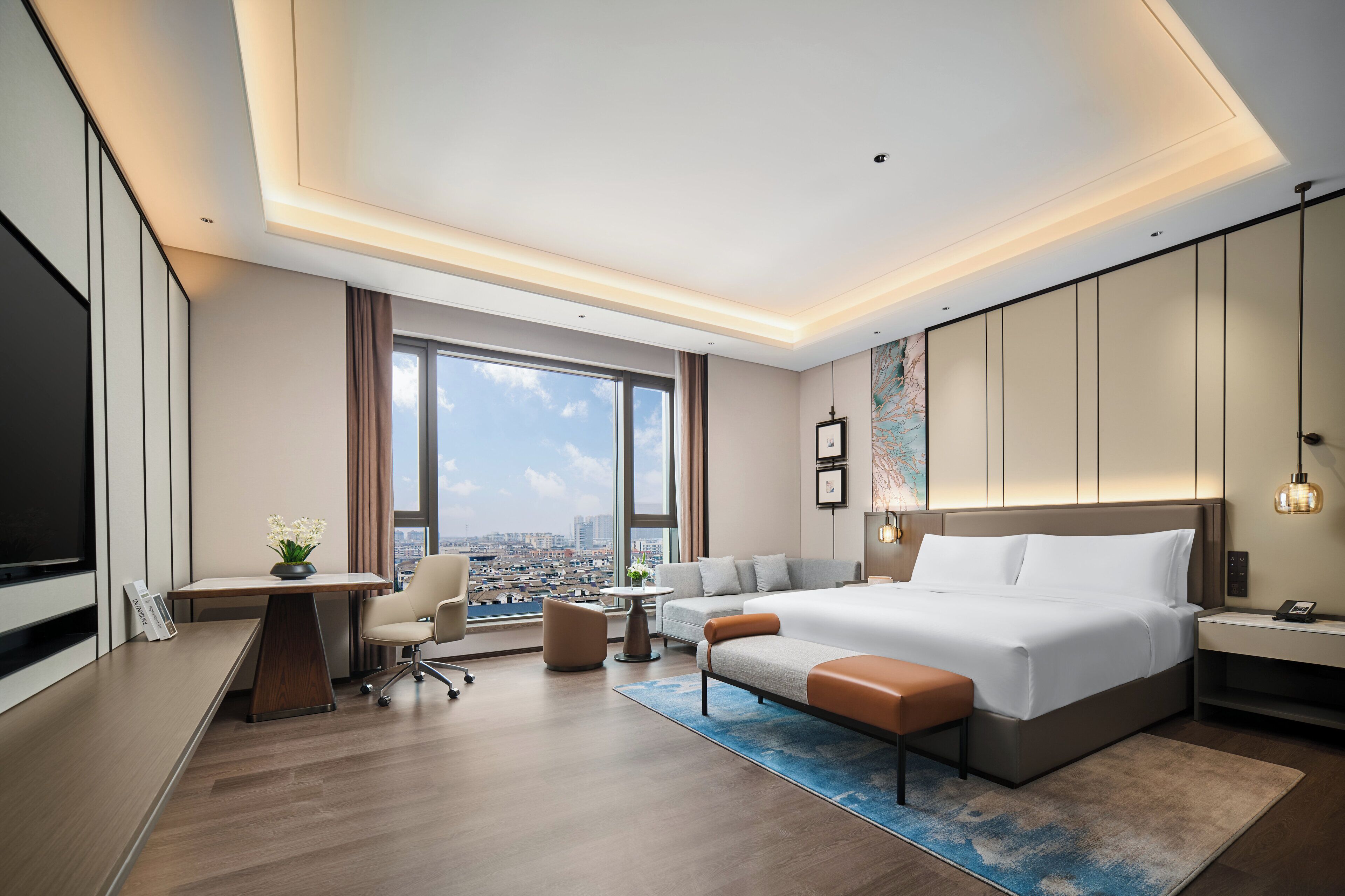 Quarto de hotel moderno com uma cama grande, uma escrivaninha, um sofá e vista para a cidade.