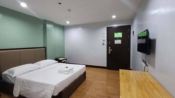 Quarto de hotel com cama, mesa de cabeceira e televisão presa na parede.
