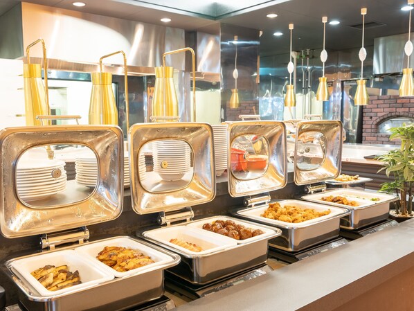 Buffet com diversas estações de comida, incluindo bandejas de carne, legumes e outros pratos.
