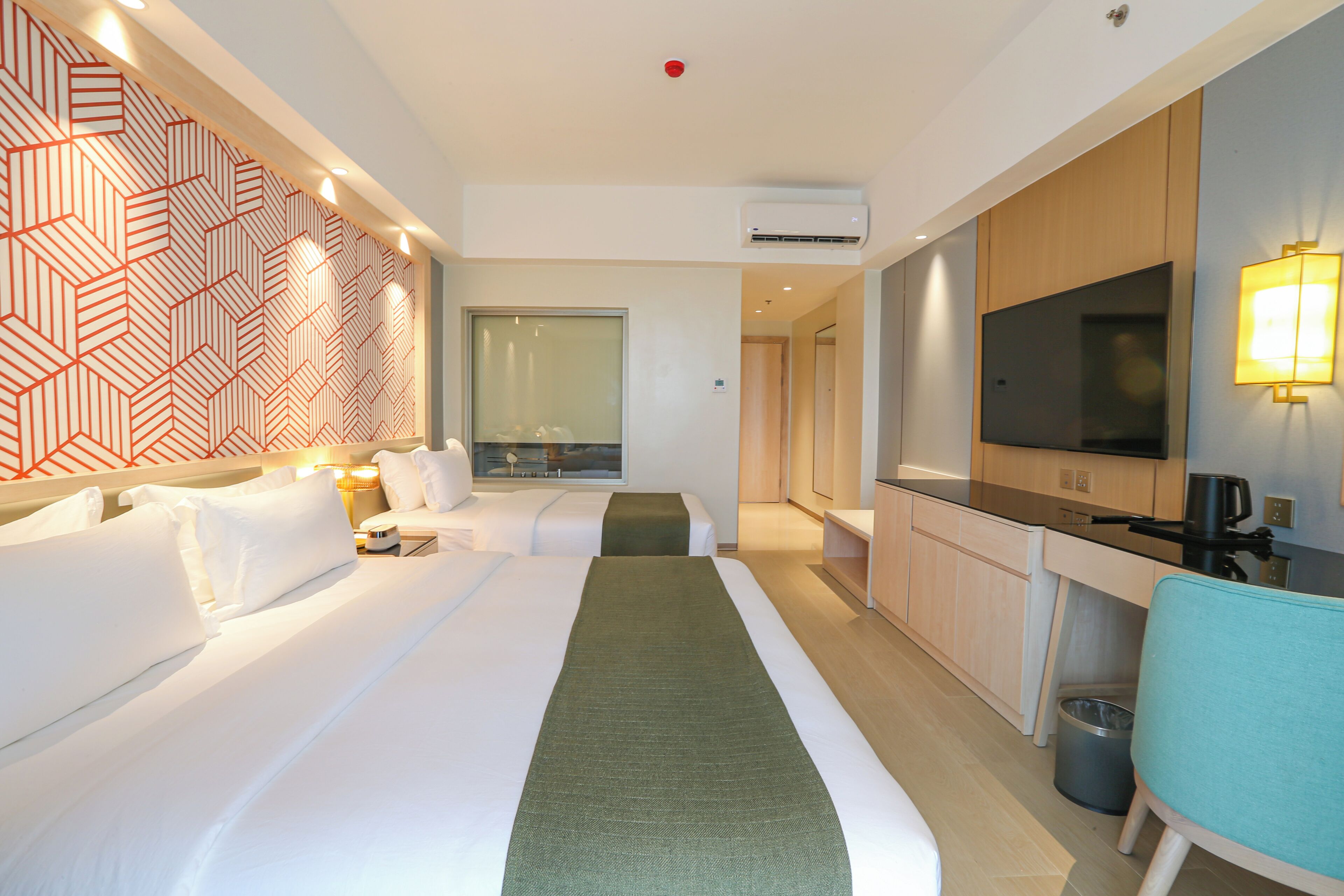 Quarto de hotel com cama, escrivaninha, televisão e banheiro visível através de uma porta de vidro.