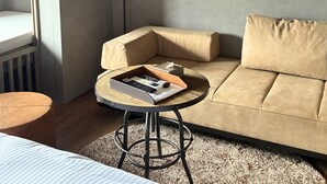 A modern living room with a beige sofa, a round coffee table with a remote control, and a striped cushion.